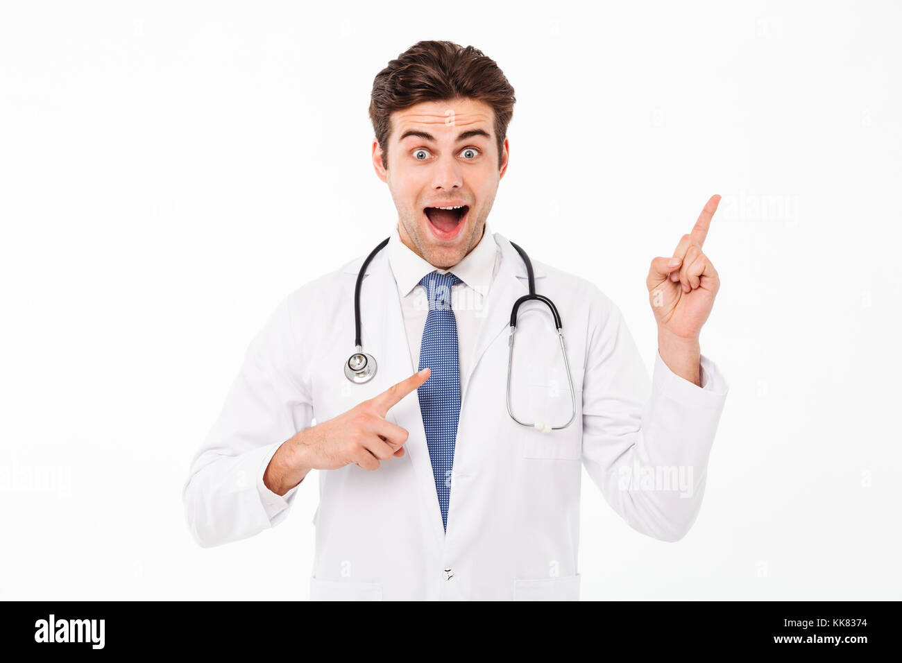 Portrait of a happy attractive male doctor dressed in uniform pointing ...