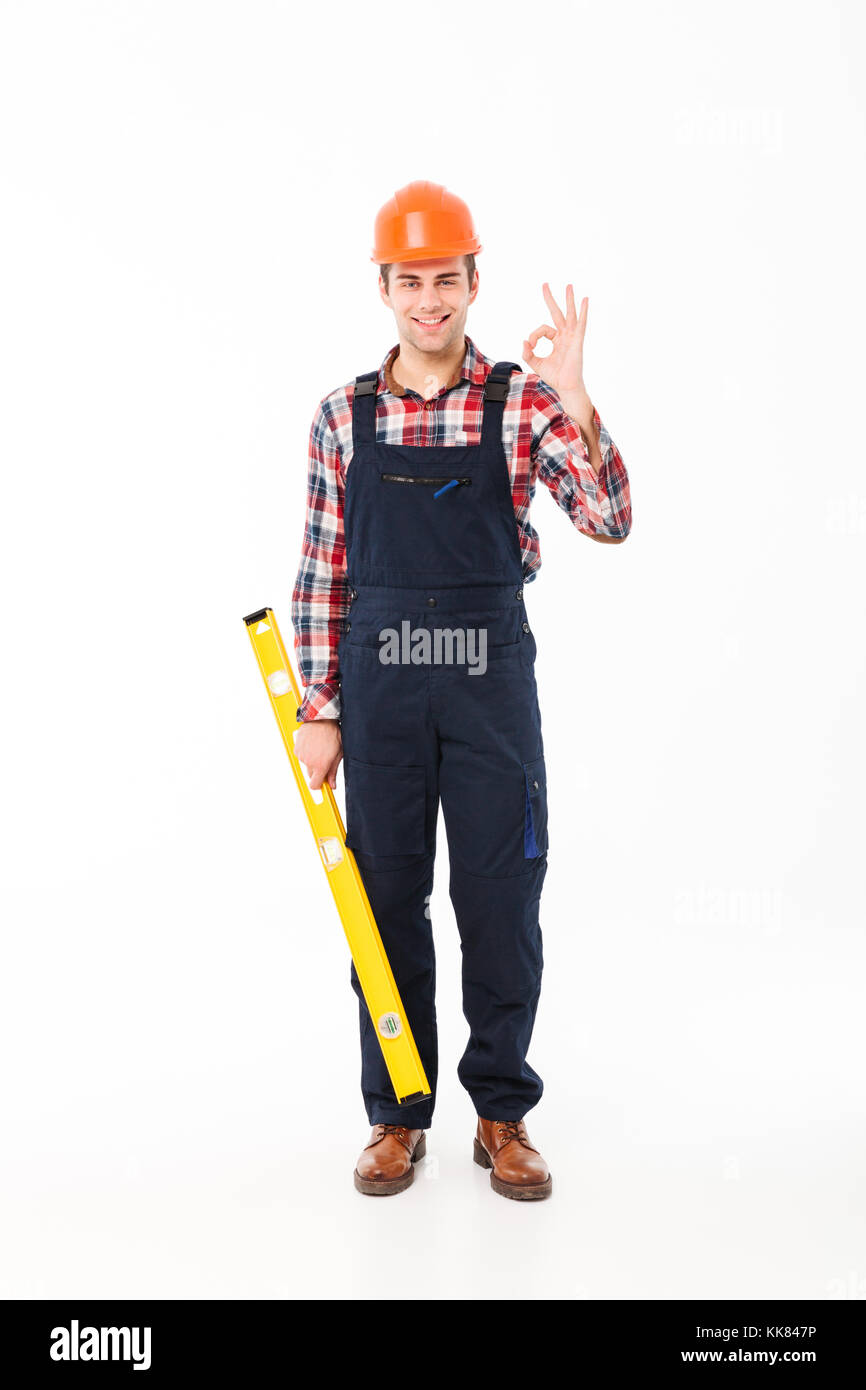 Full length portrait of a cheerful young male builder holding spirit ...