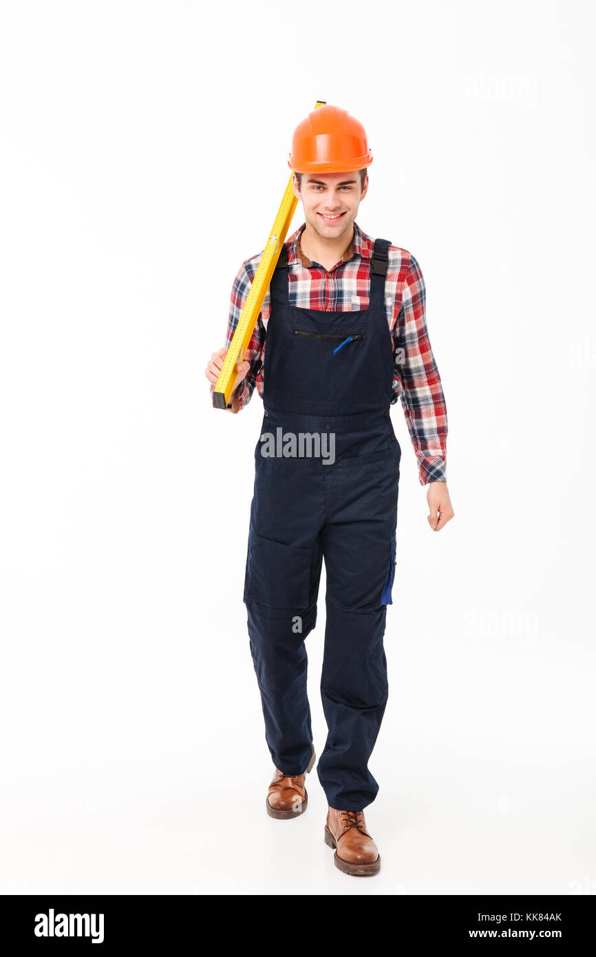 Full length portrait of a happy young male builder holding spirit level ...