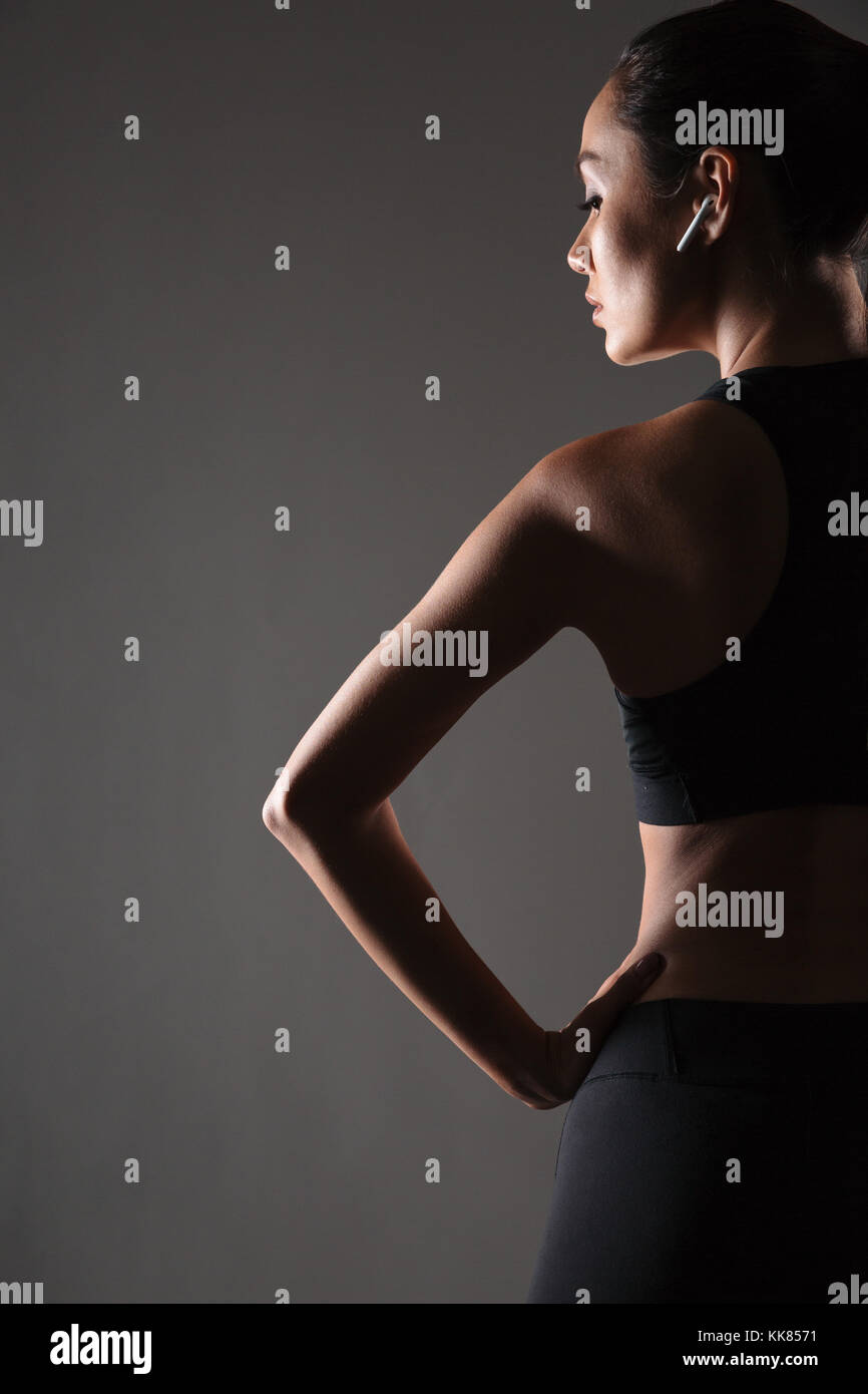 Back view half body of a young fitness woman standing with hand oh hip ...