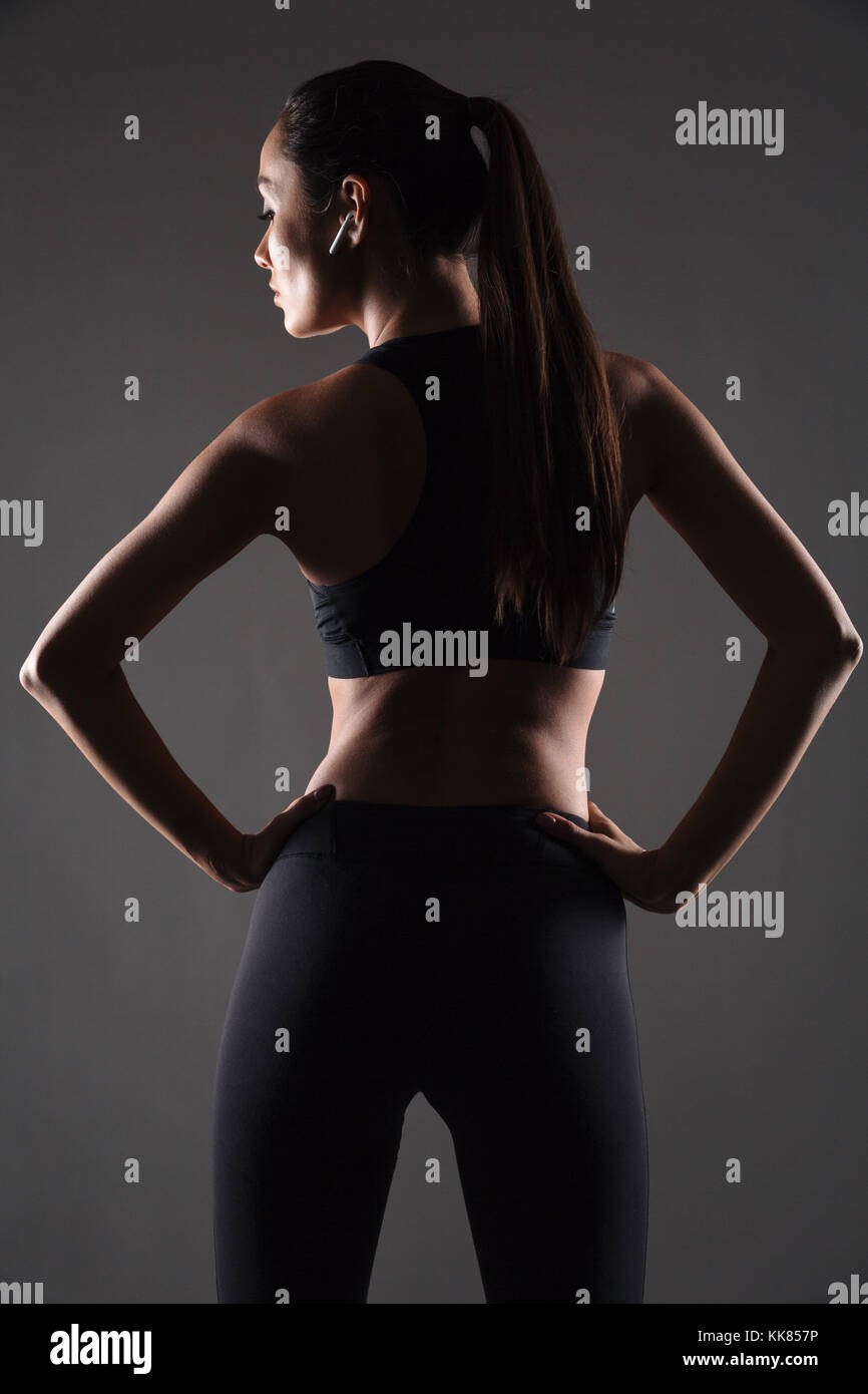 Back view portrait of a young fitness woman standing with hands oh hips ...