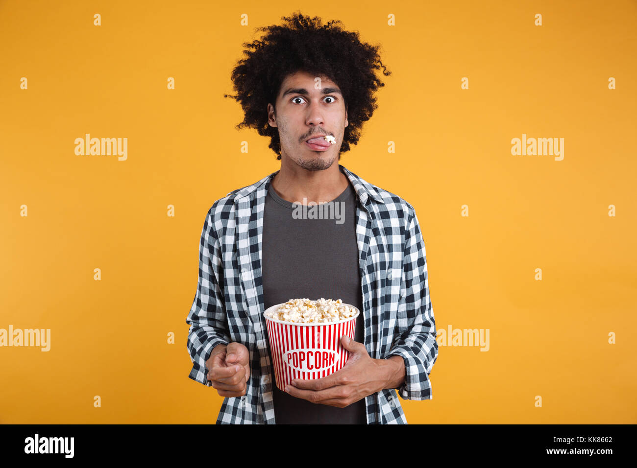 Portrait of a funny afro american man eating popcorn isolated over ...