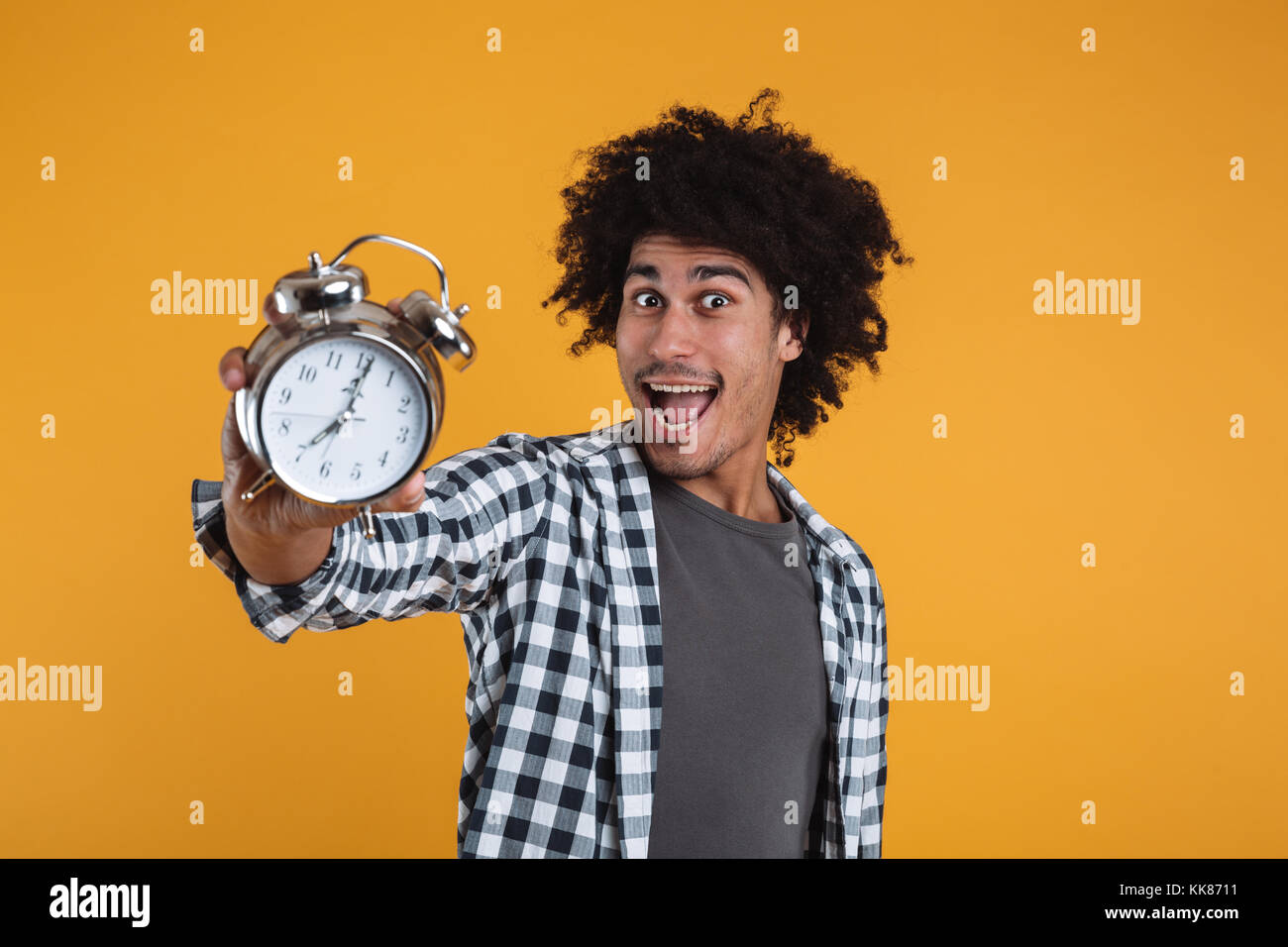 Portrait of a happy excited african man showing alarm clock isolated ...