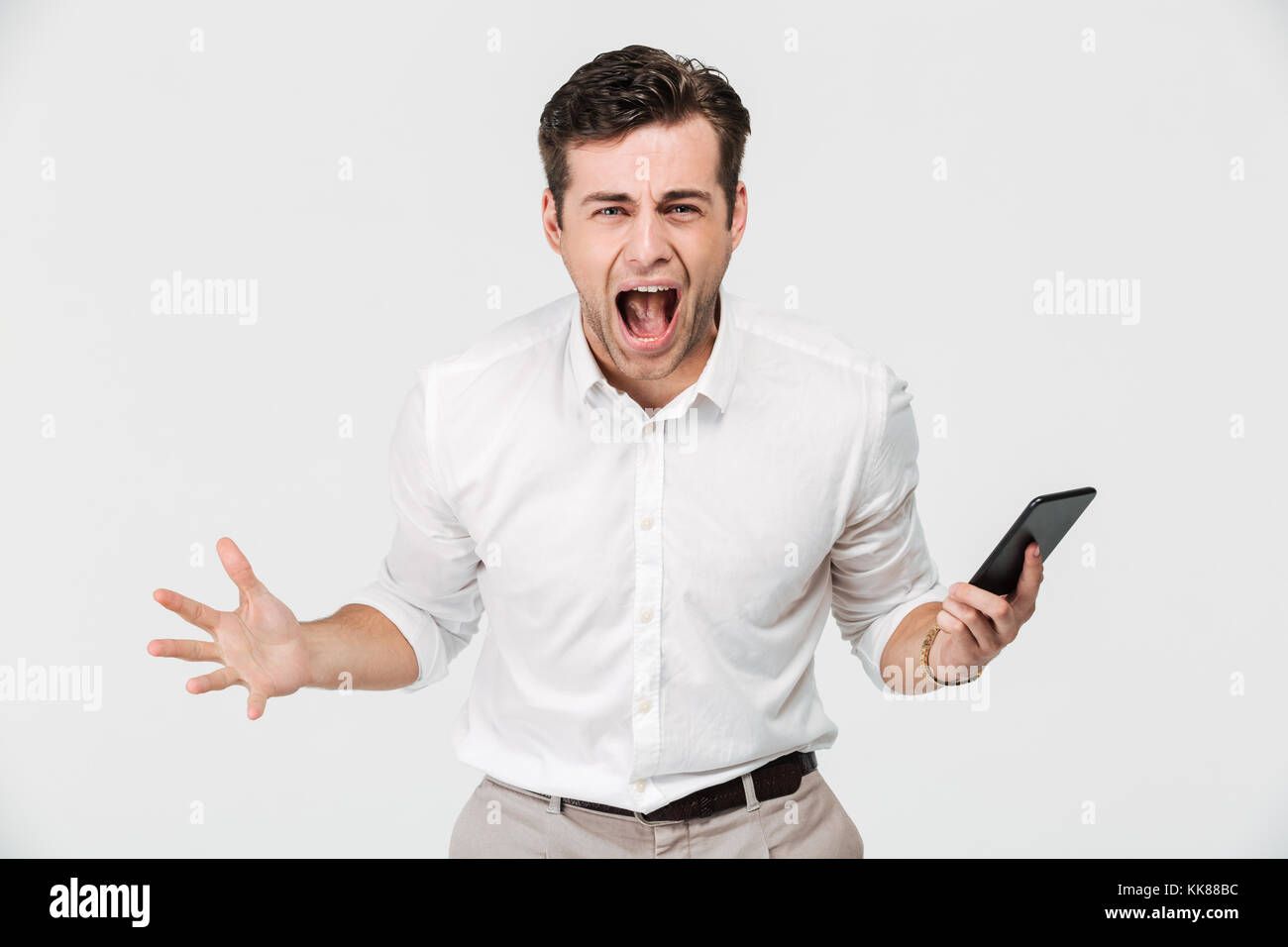 Portrait of a crazy angry man holding mobile phone and shouting ...