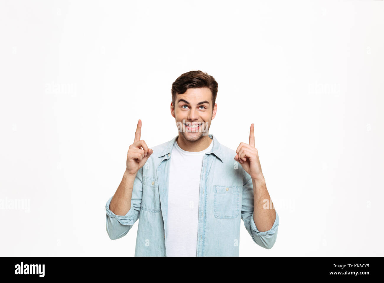 Portrait of a happy young man standing and pointing two fingers up ...