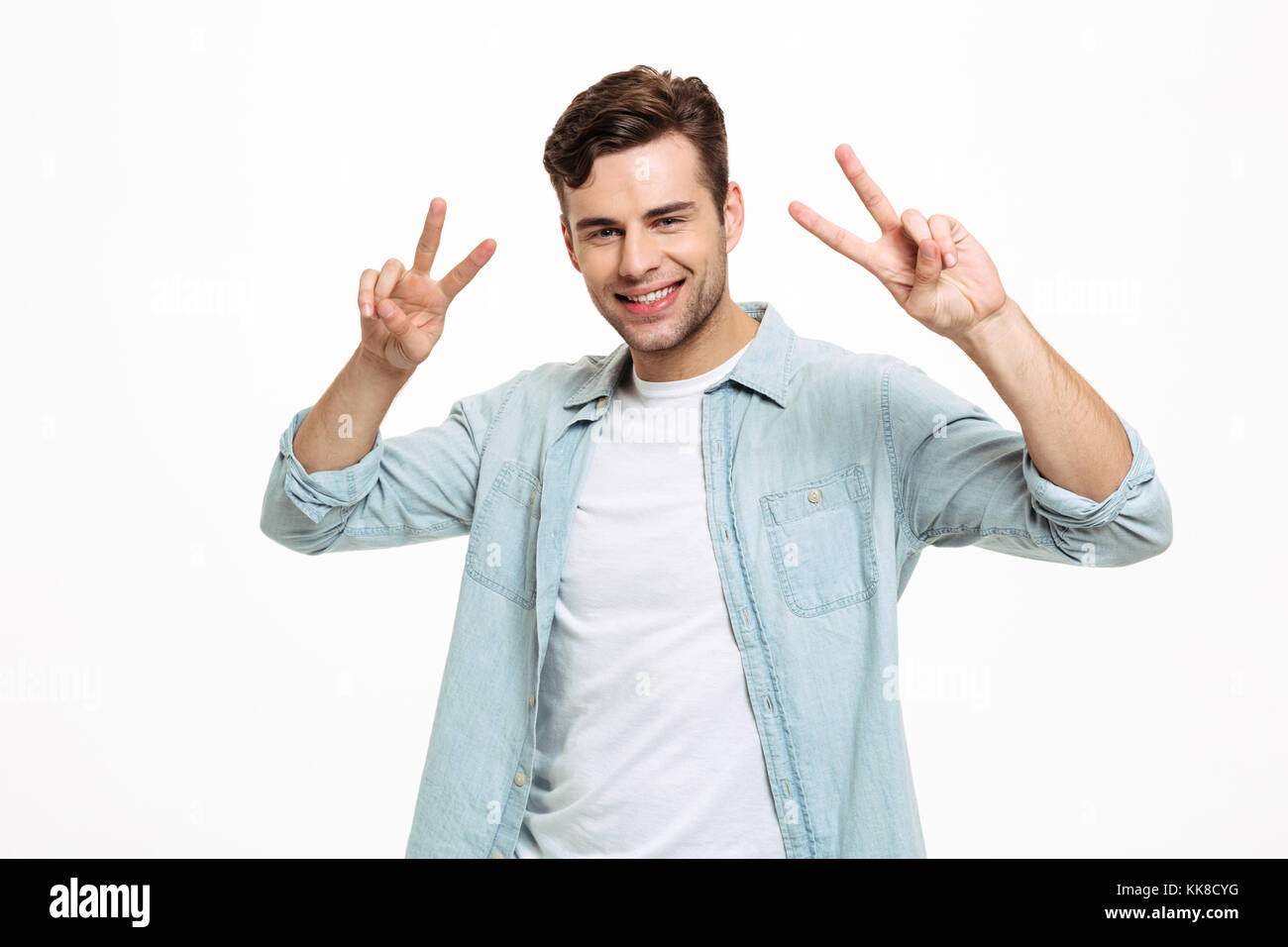 Portrait of a pleased smiling man standing and showing peace gesture ...