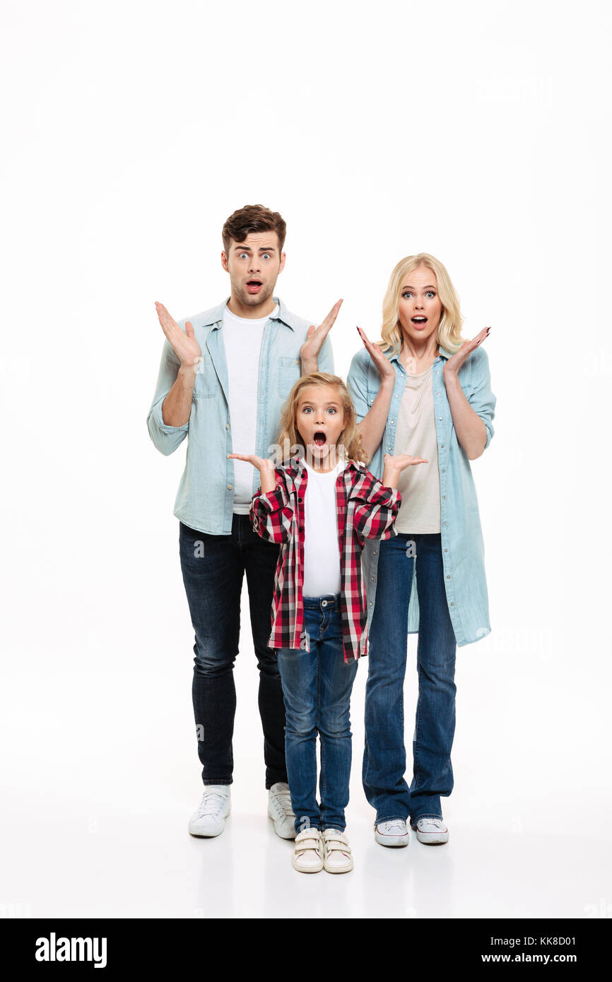 Full length portrait of a shocked young family standing and gesturing ...