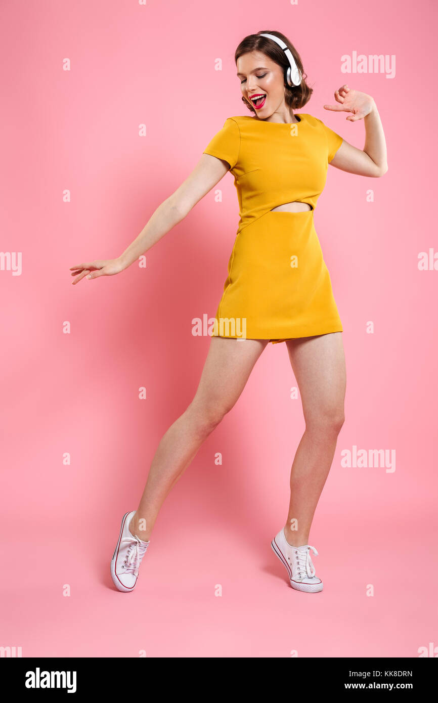 Picture of excited smiling young lady in yellow dress dancing isolated ...