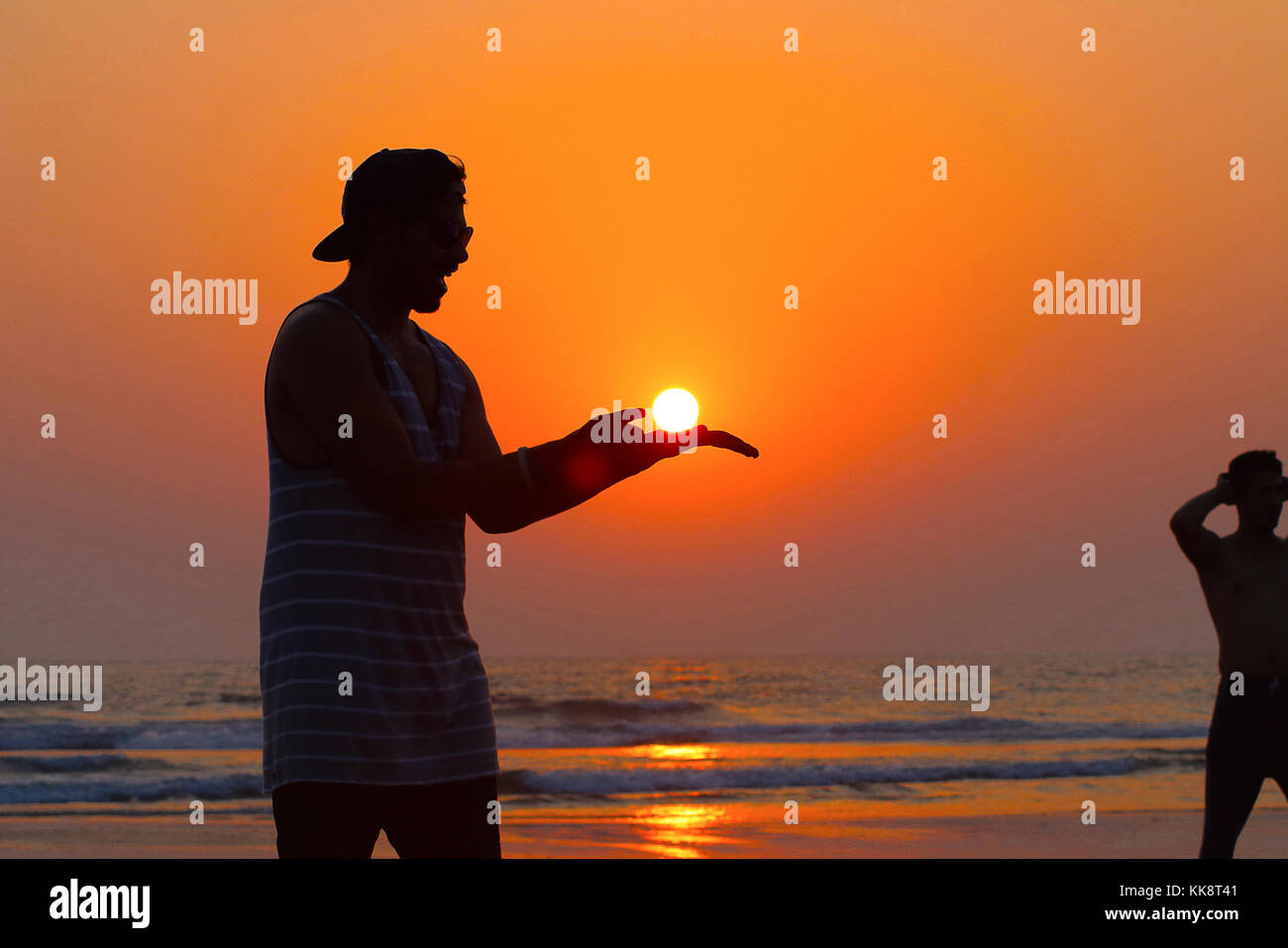 Man wearing a cap and cooling glasses posing as if holding the sun in ...