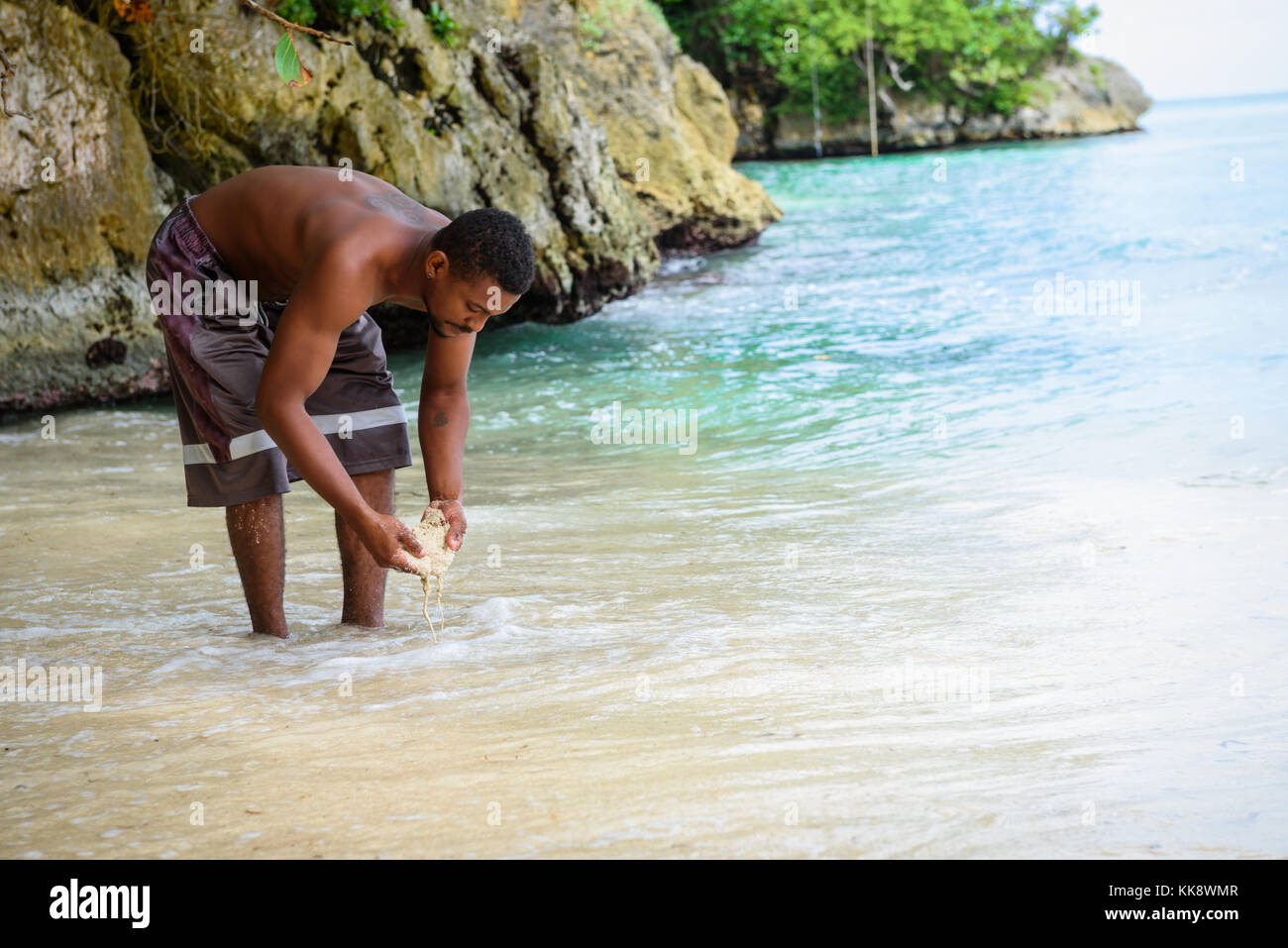 Man playing with sand on a caribbean beach with blue ocean and rocks in ...