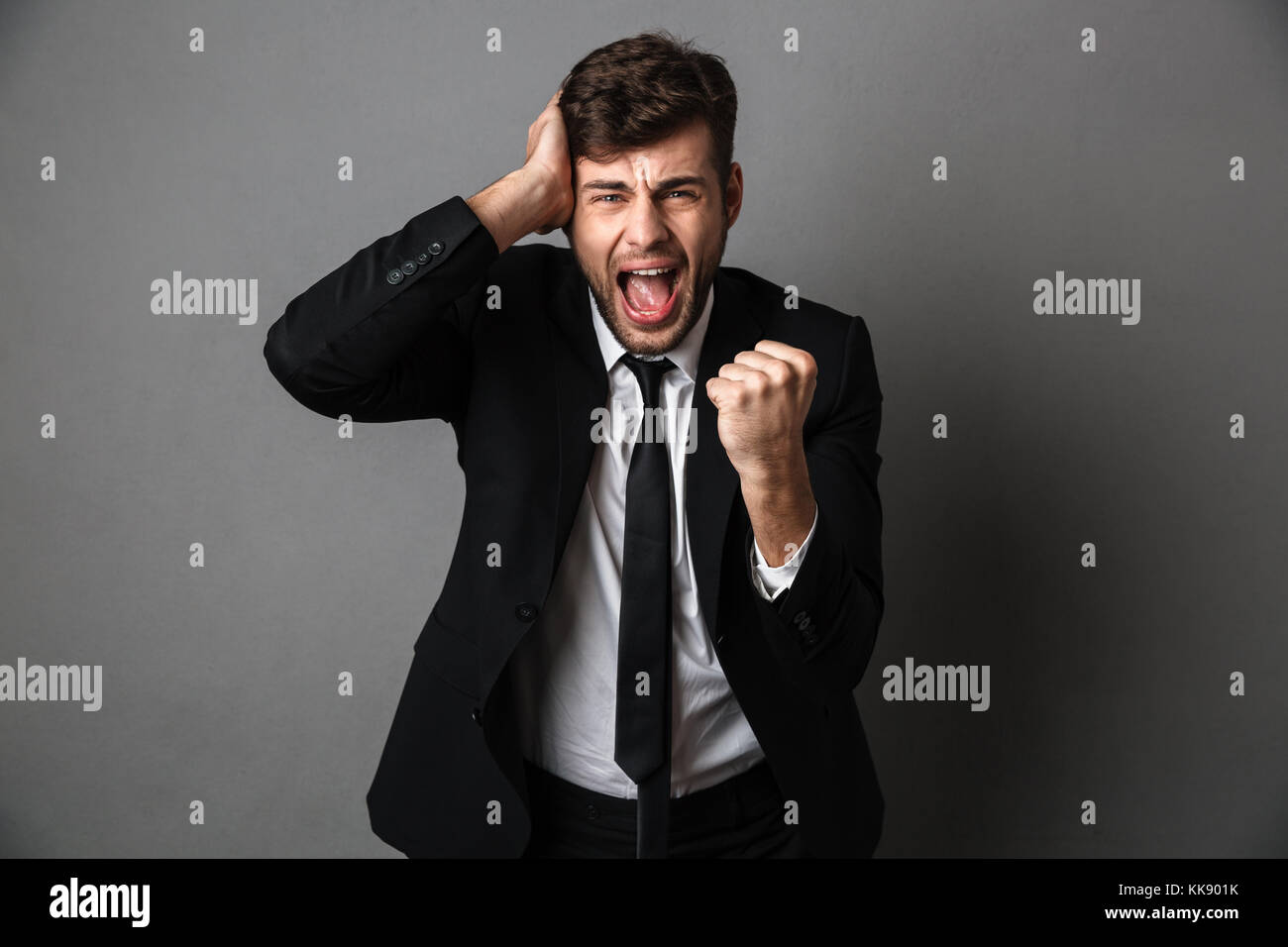 Close-up photo of angry screaming young man in black suit covering his ...