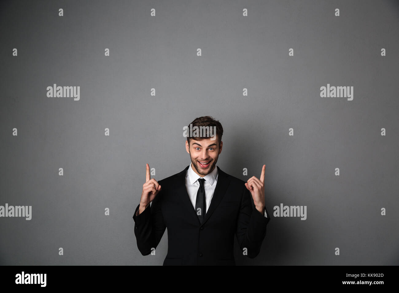 Close-up photo of young smiling man in formal wear pointing with two ...