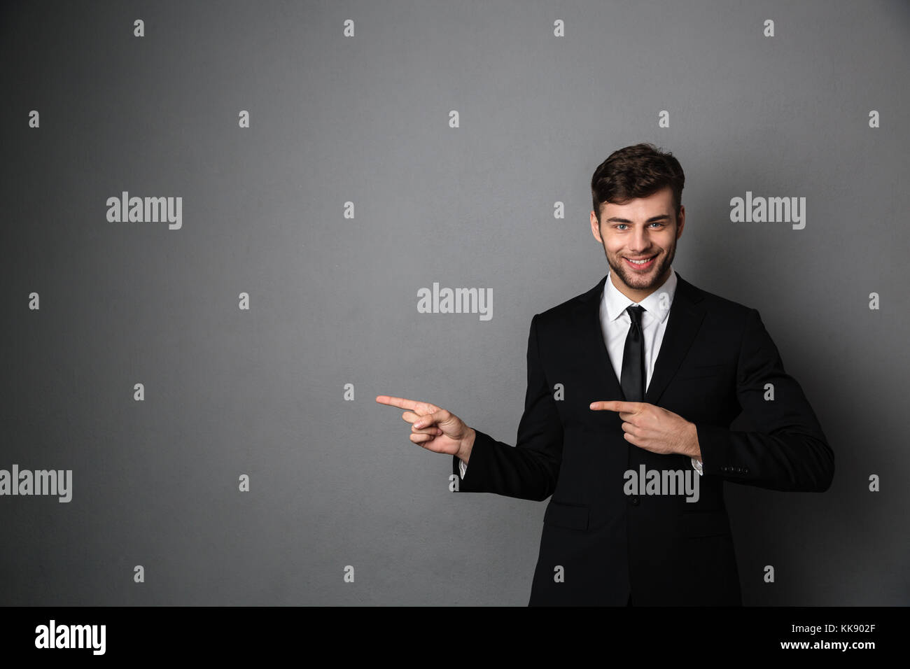 Cheerful brunette bearded man in formal wear pointing with two fingers ...