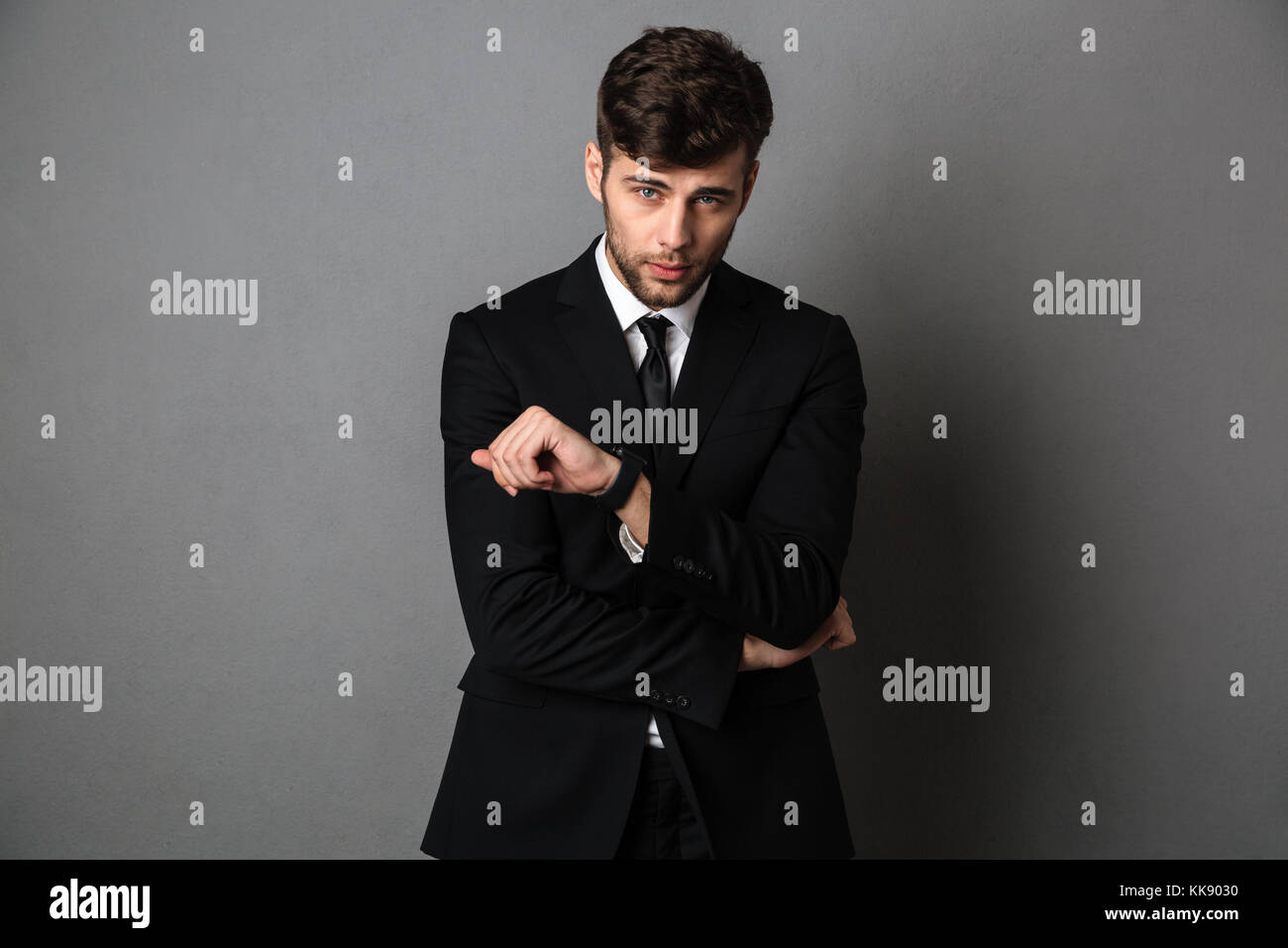 Serious hansome guy in black suit checking time on his wristwatch ...