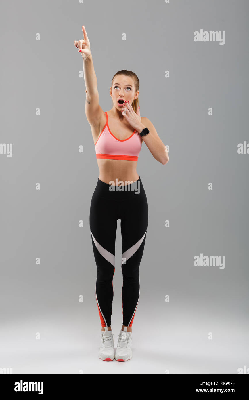 Full length portrait of an amazed young sports girl pointing finger up ...