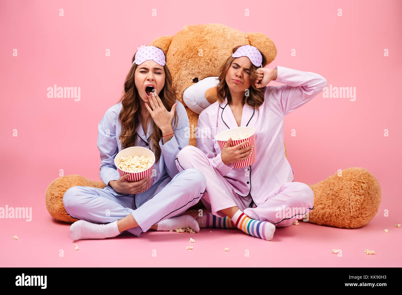 Two sleepy pretty girls dressed in pajamas sitting with a big teddy ...