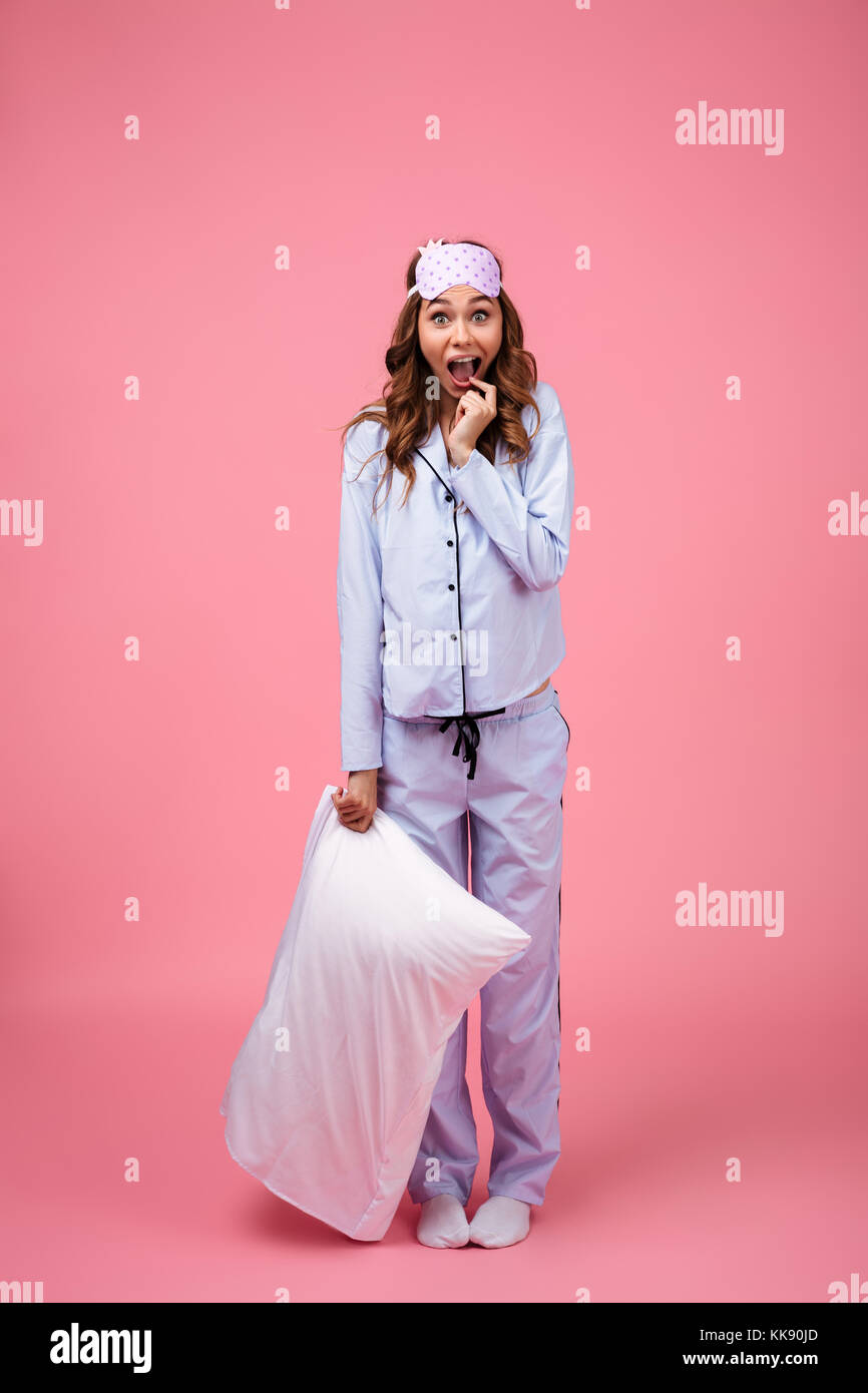 Full length portrait of a shocked young girl dressed in pajamas holding ...