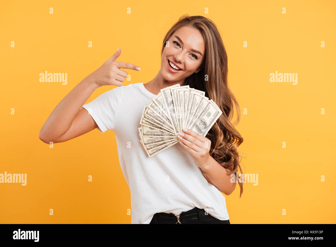 Portrait of a happy cheerful girl pointing finger at bunch of money ...