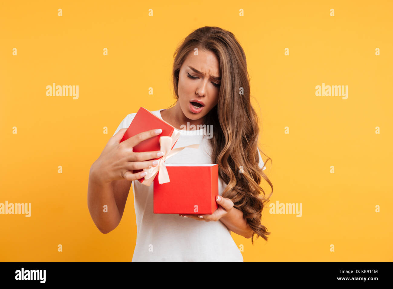 Portrait of an upset disappointed girl opening gift box isolated over ...