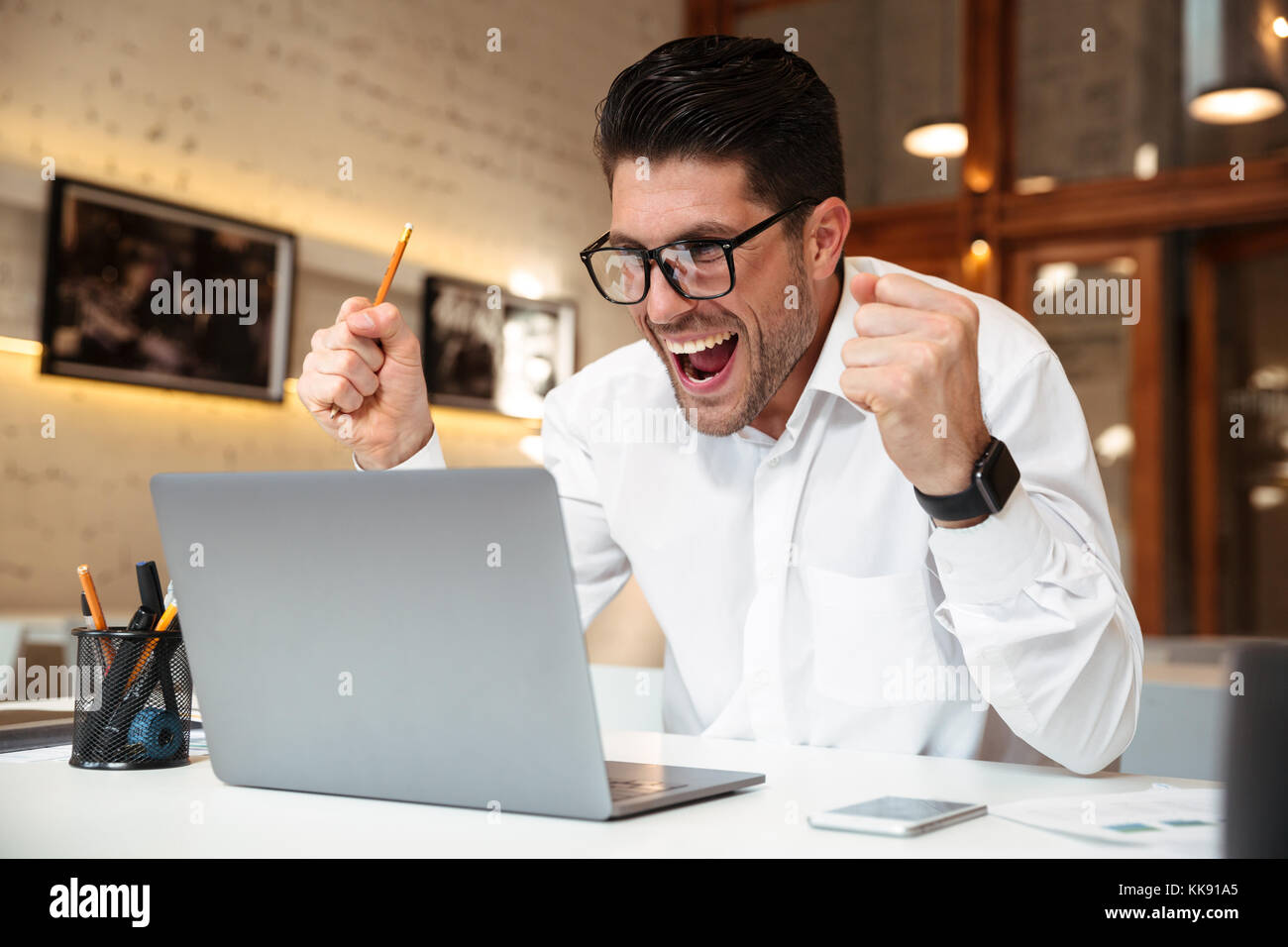 Young happy business man showing winner gesture, looking at laptop ...