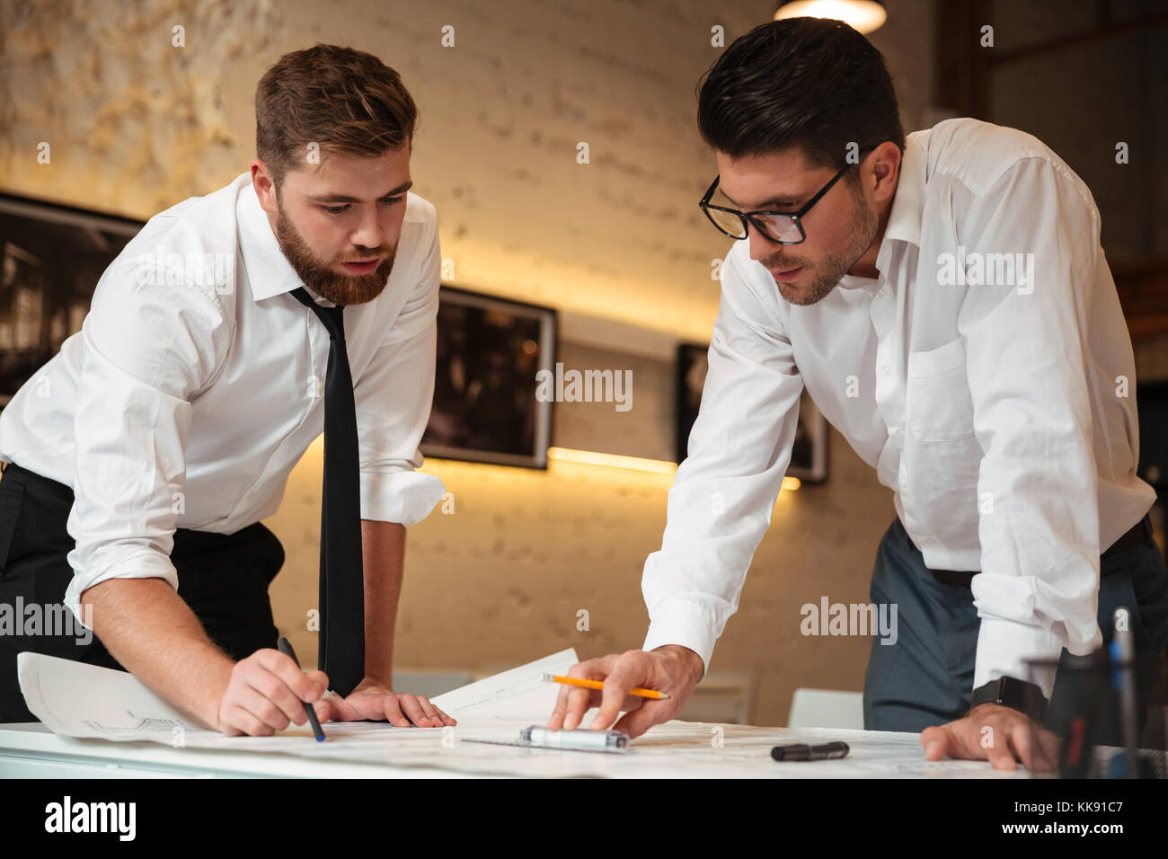 Two young smart businessmen working on a business plan while standing ...