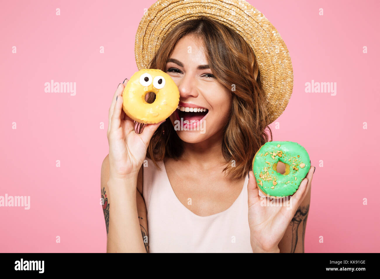 Close up portrait of a funny smiling woman in summer hat holding donut ...