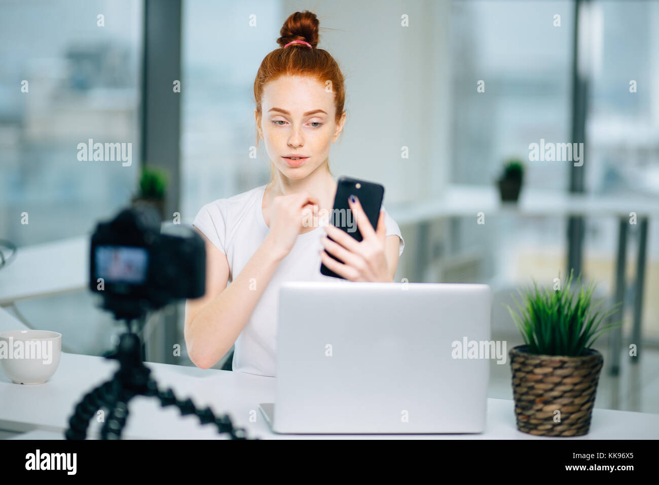 Young female redhead blogger with laptop recording video at home and ...