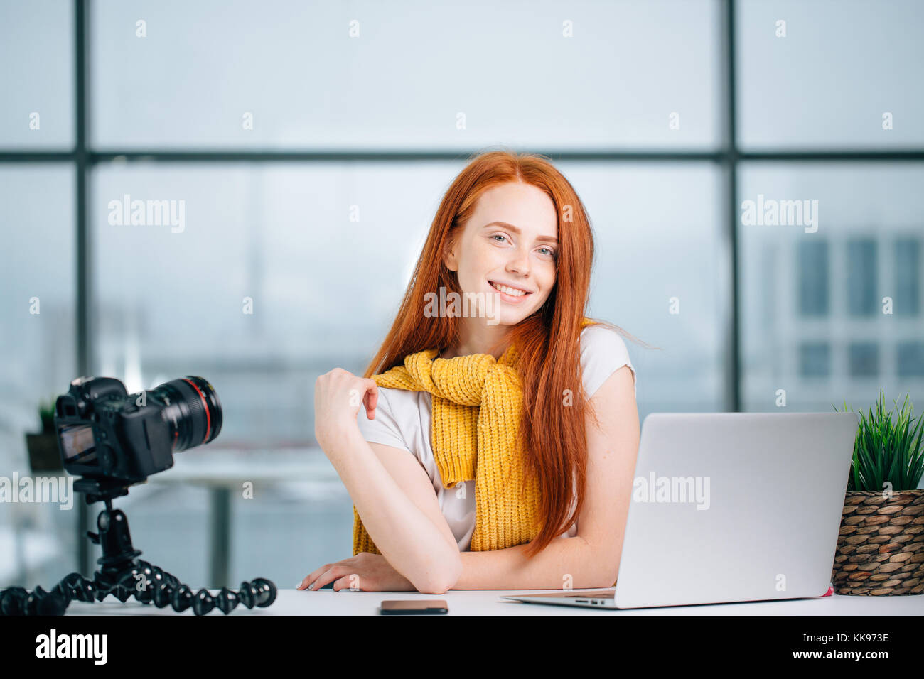 Young female blogger with laptop and book on camera screen looking at ...