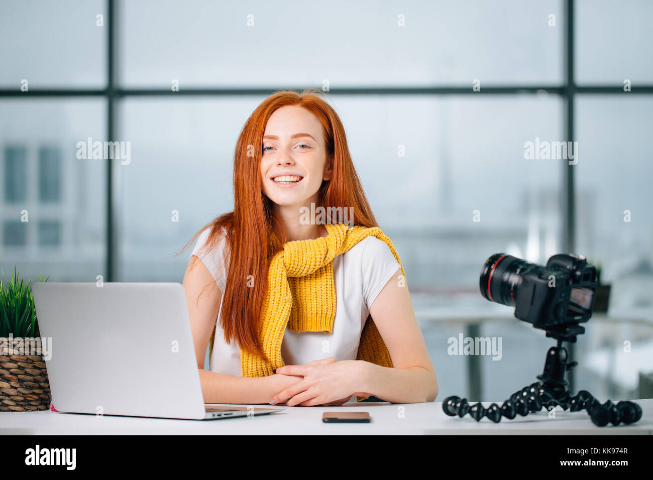 Young female blogger with laptop and book on camera screen looking at ...