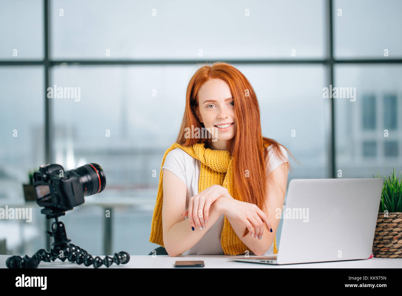 Young female blogger with laptop and book on camera screen looking at ...