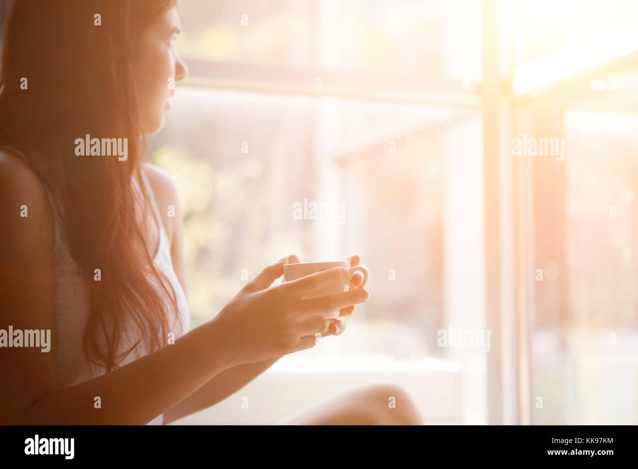 Romantic photo of long-haired girl with cup of tea by window in room ...