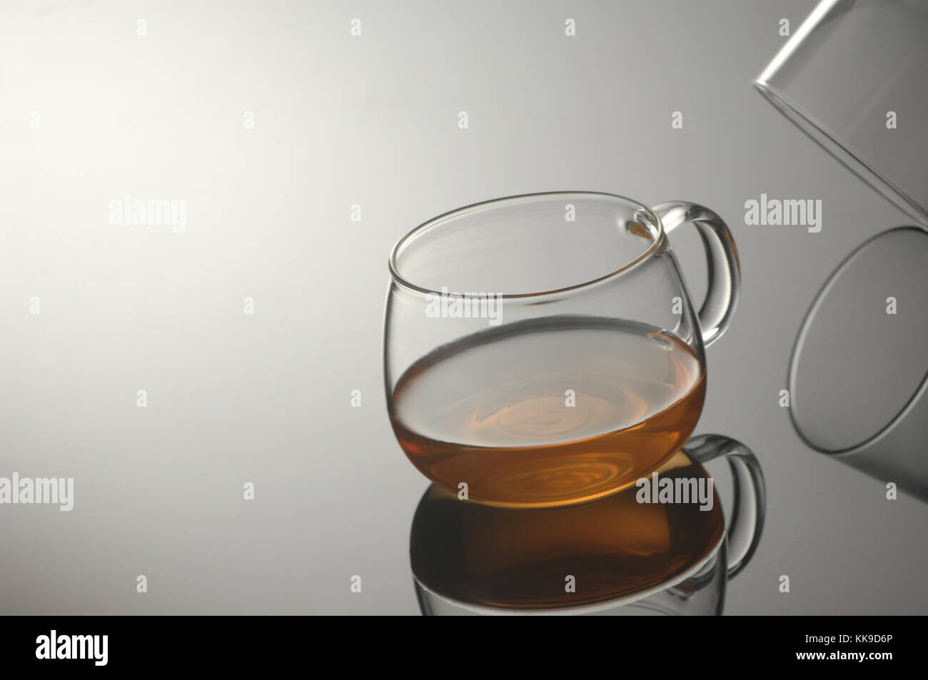 A transparent glass cup with tea on a reflecting surface and a light ...
