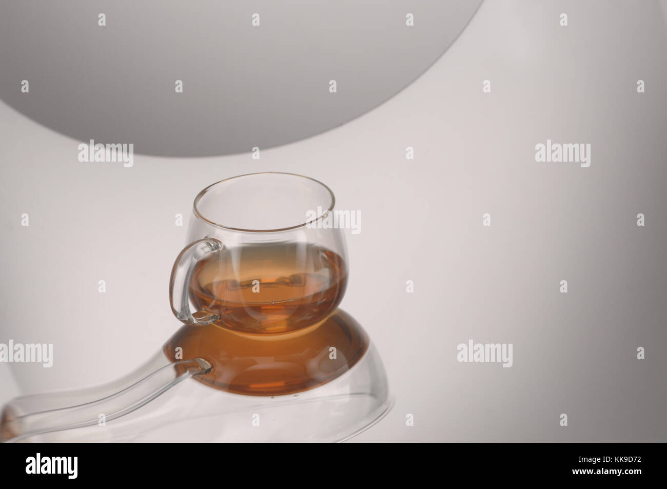 A transparent glass cup with tea on a reflecting surface and a light ...