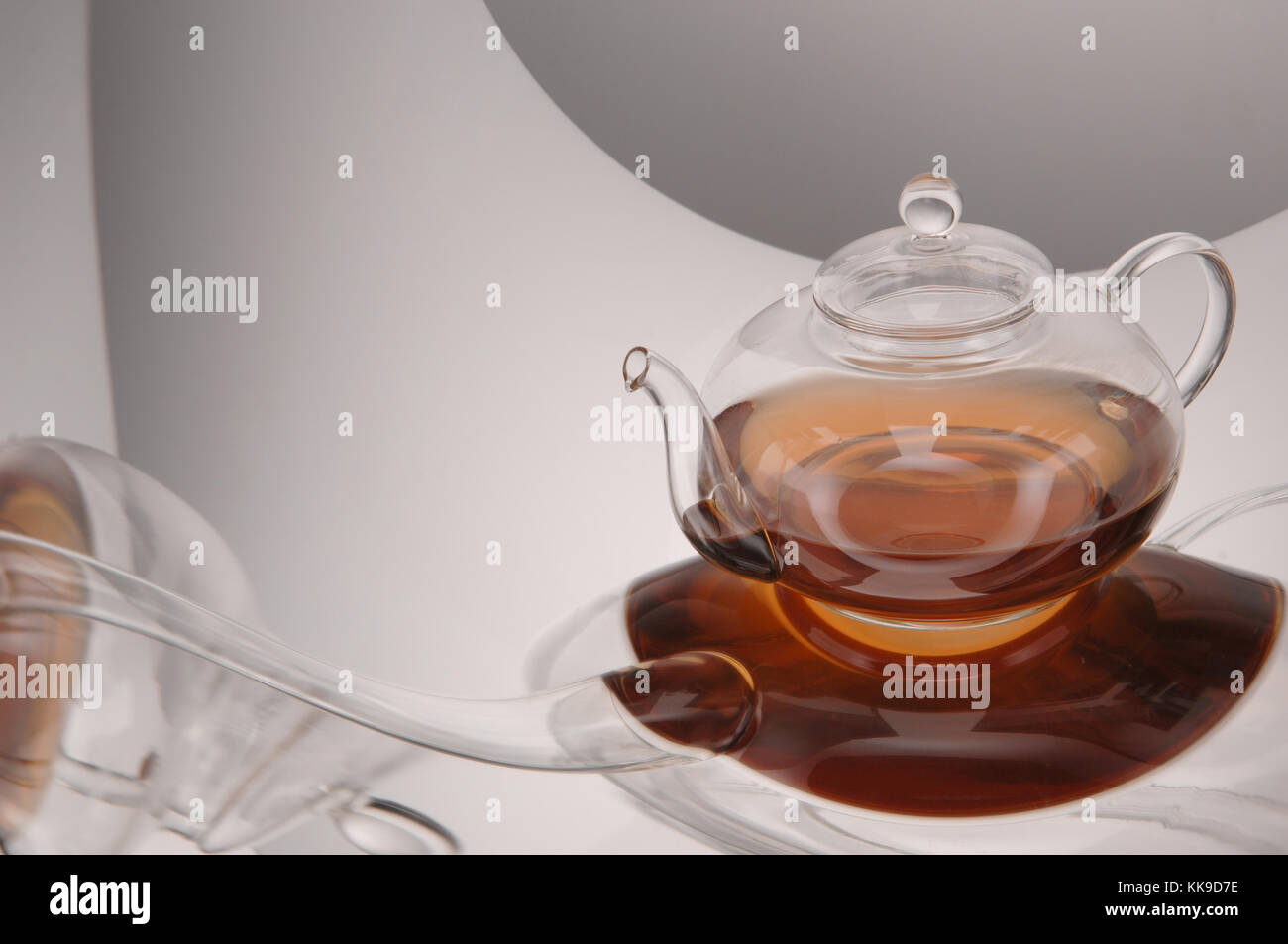 Transparent glass teapot with tea on the reflective surface on a light ...
