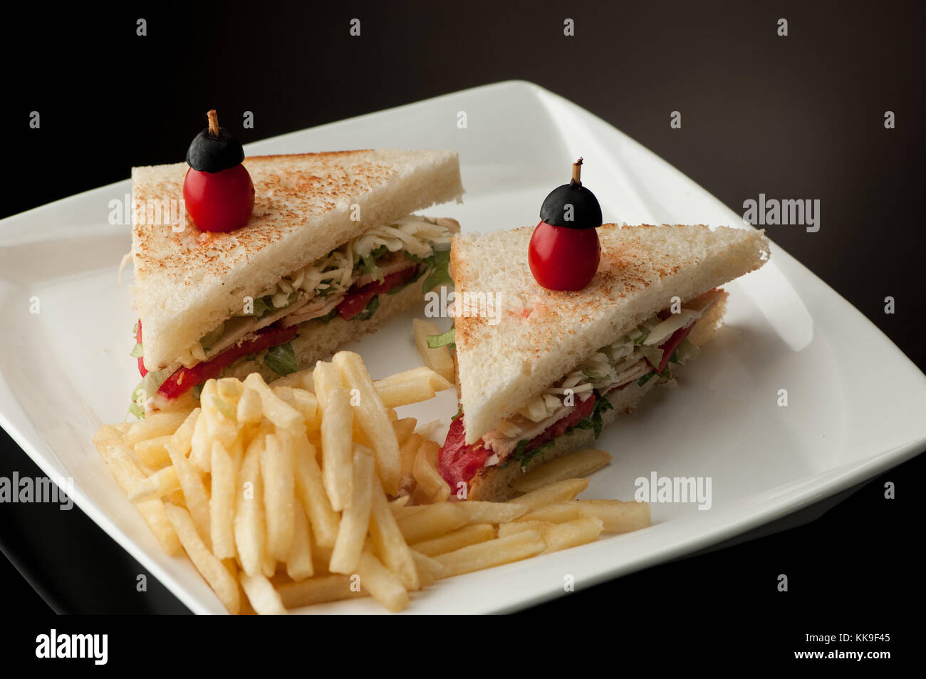two sandwiches in a square white plate with fries Stock Photo - Alamy