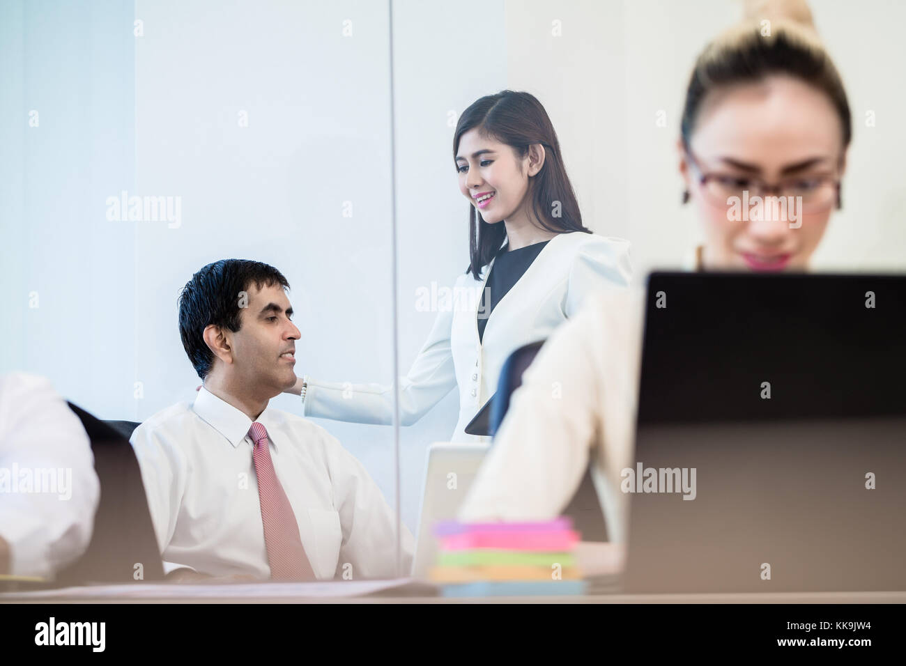 Office co-workers talking gossip behind back of Asian business woman ...