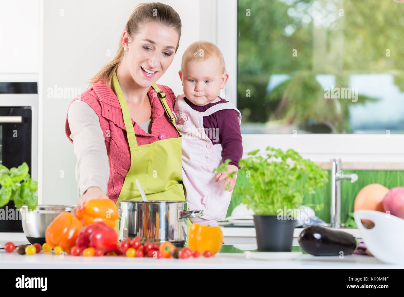 Mother working and cooking in kitchen while carrying child Stock Photo ...