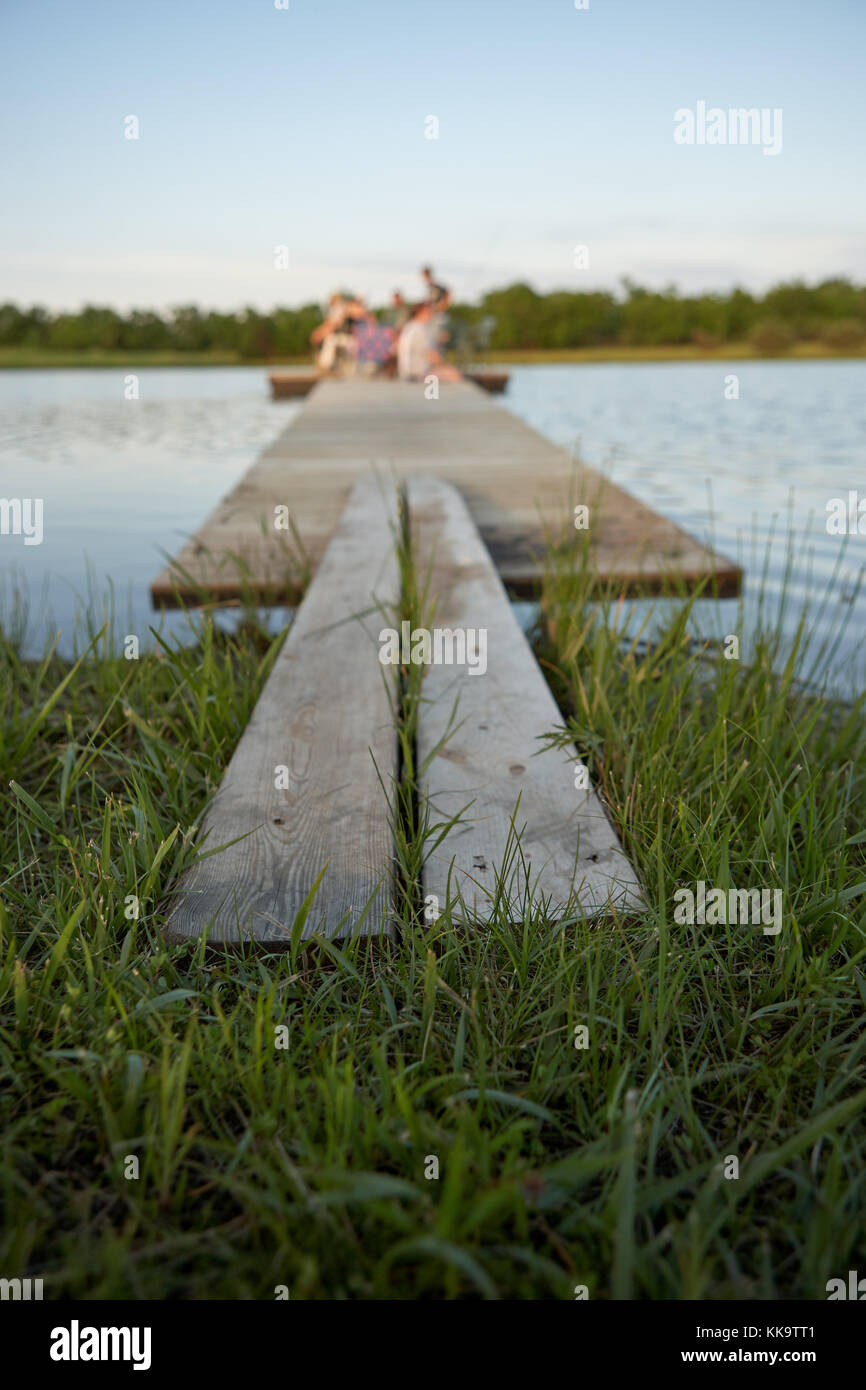 Low angle view along a rustic wooden jetty with people relaxing at the ...