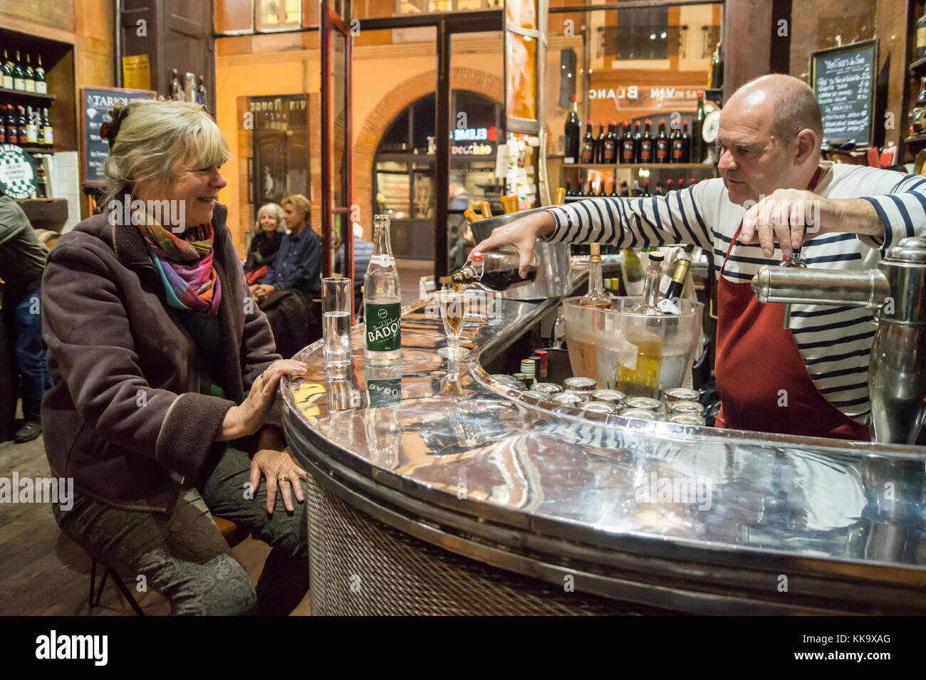Barman pouring quinquina aperitif for a seated woman, Au Père Louis bar ...