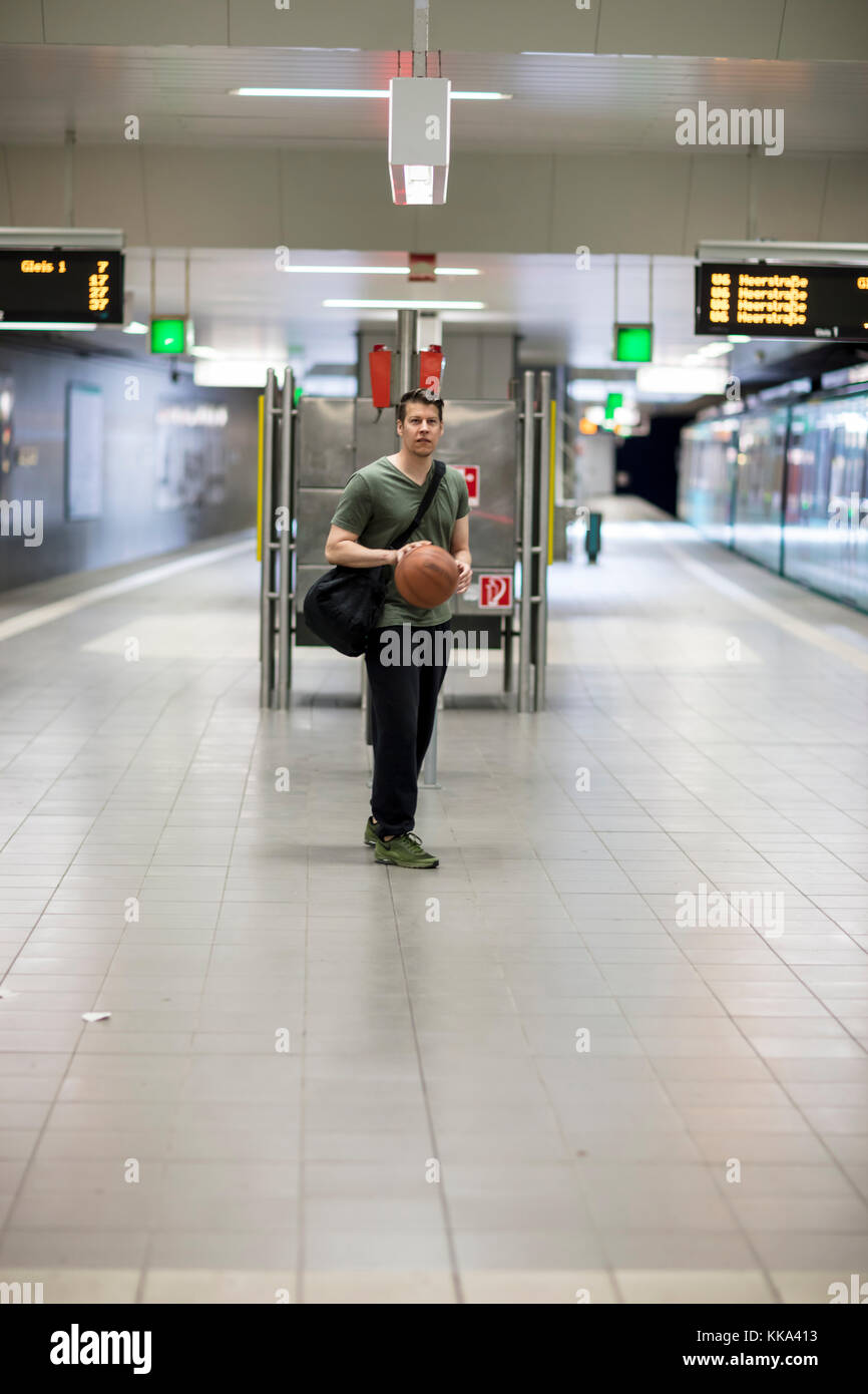 A man with a basketball and dressed in activewear standing at a subway ...