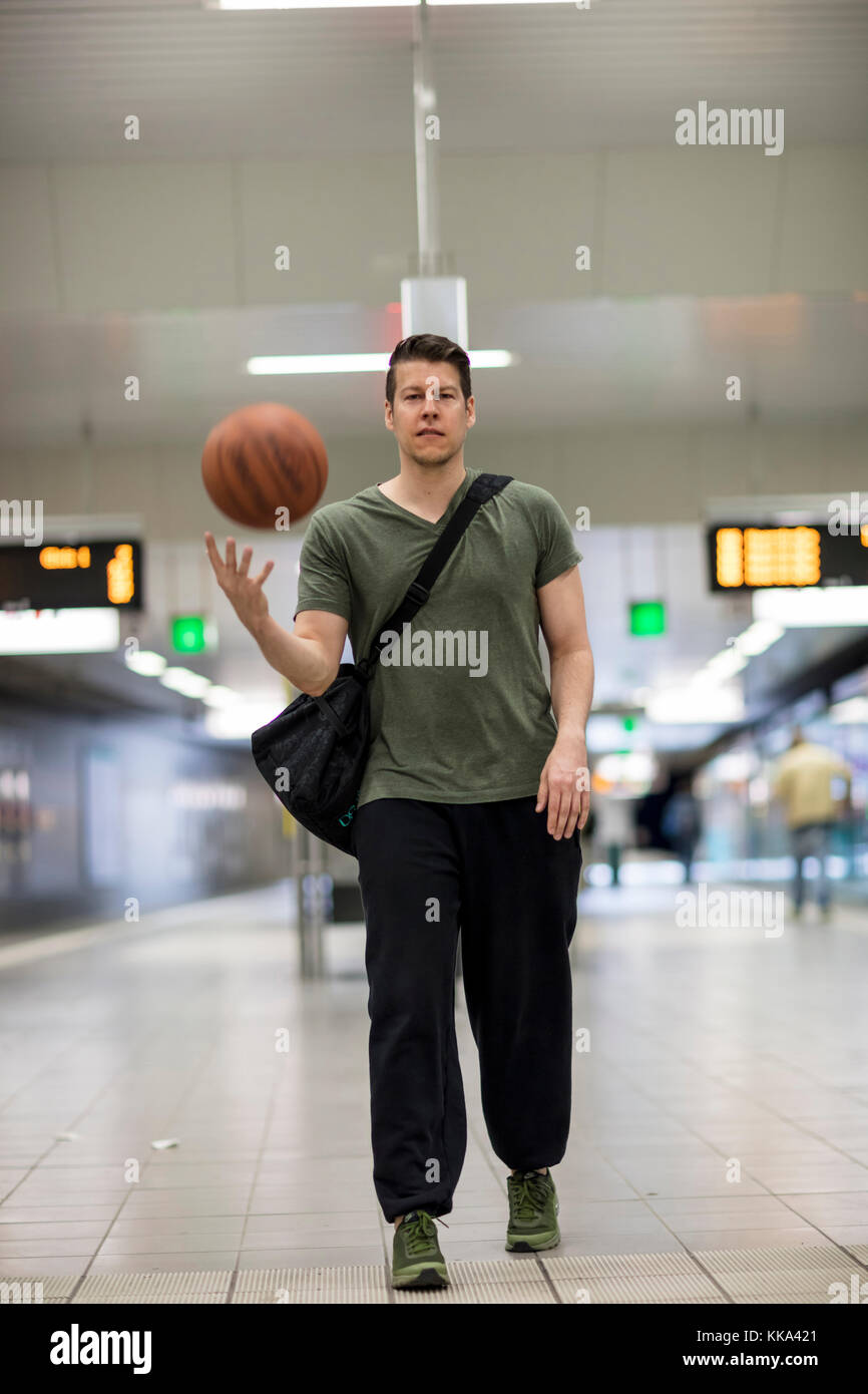 A man with a basketball and dressed in activewear standing at a subway ...