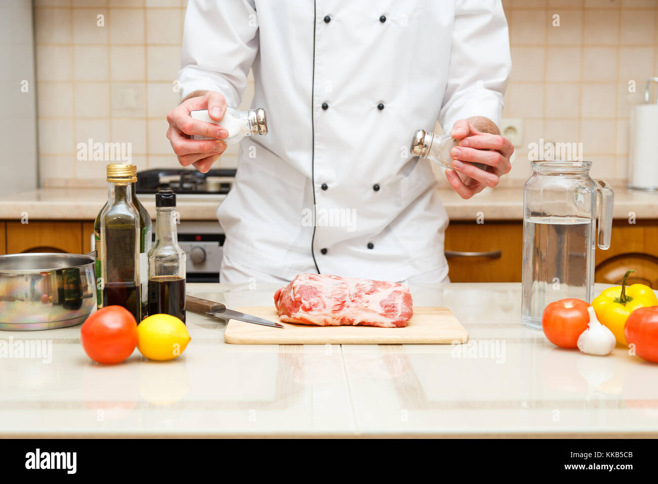 A man chef sprinkles salt and pepper from shakers cooking the meat ...