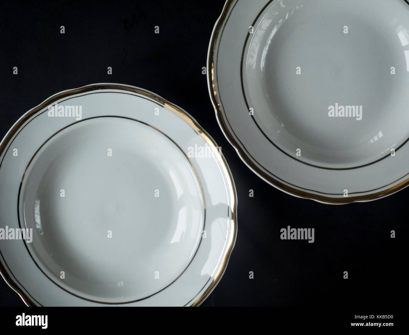 high above view of two white plates with gold border isolated on black ...