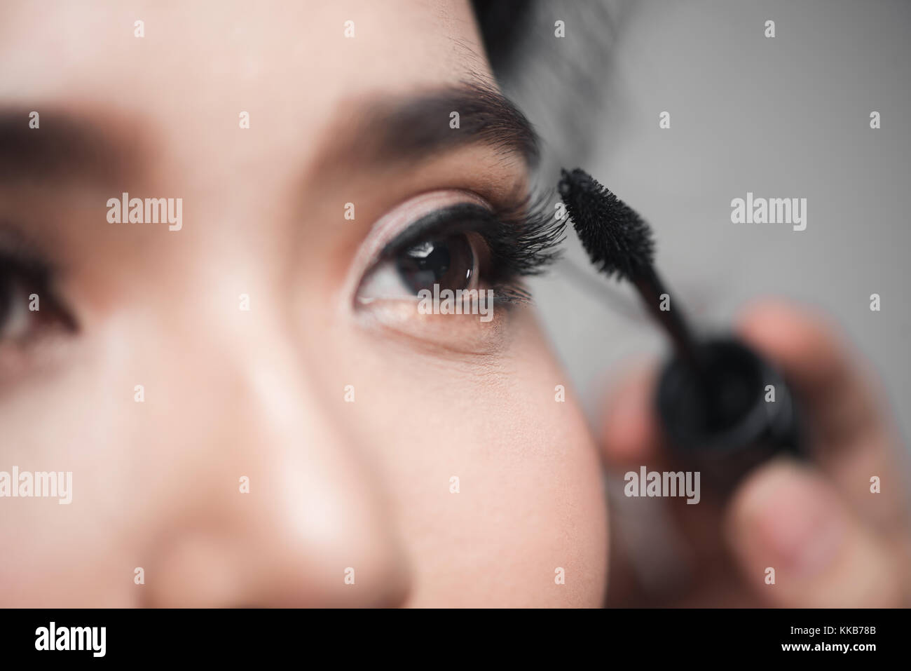Close-up portrait of beautiful girl touching black mascara to her ...
