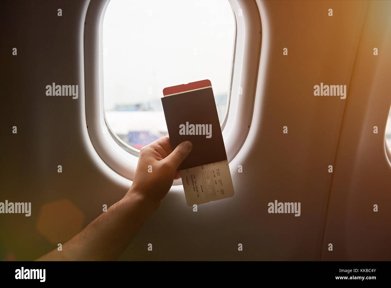 Hand holding passport with airplane ticket on plane window sunny ...