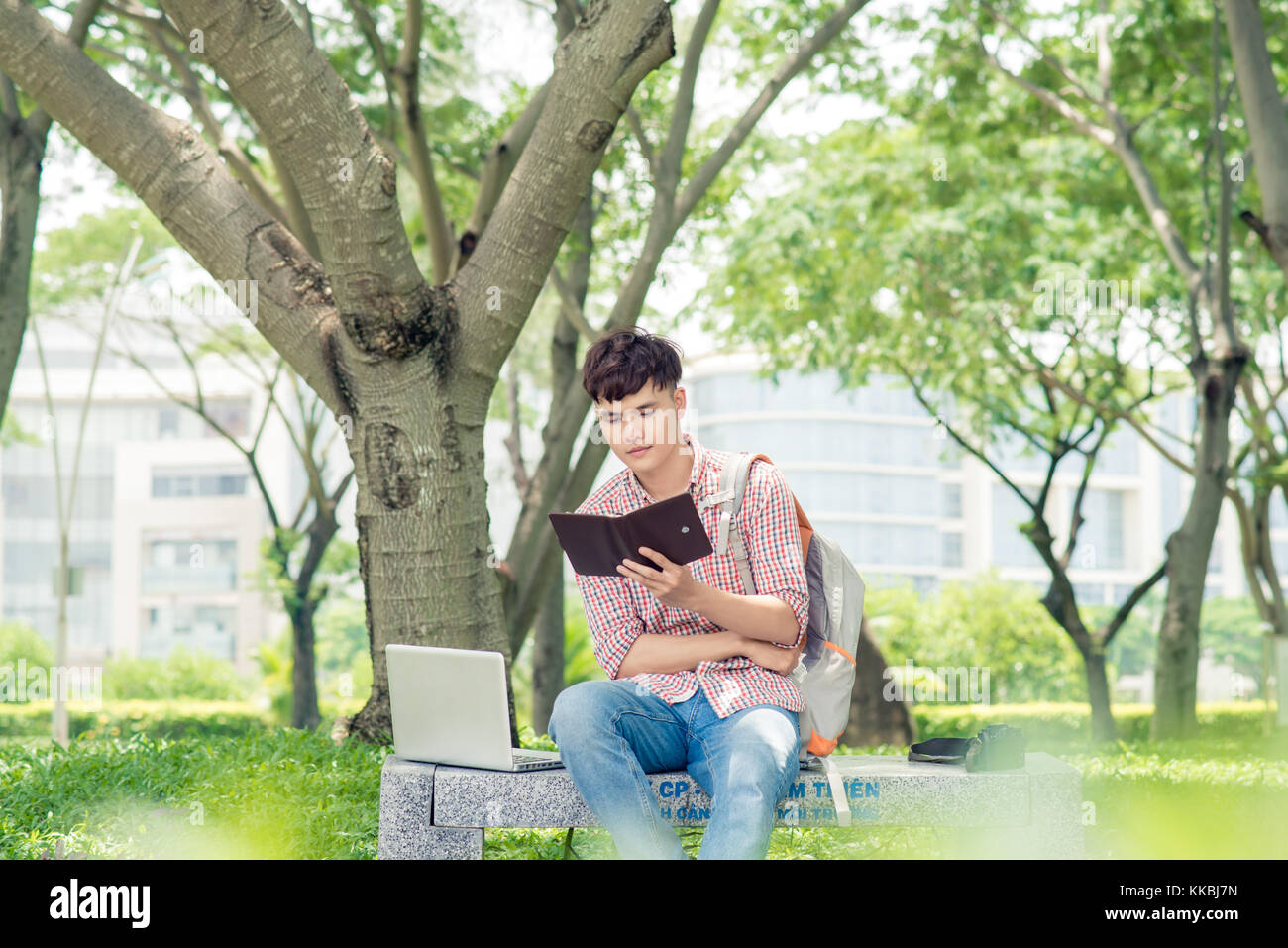 Young asian man with backpack reading a book Stock Photo - Alamy