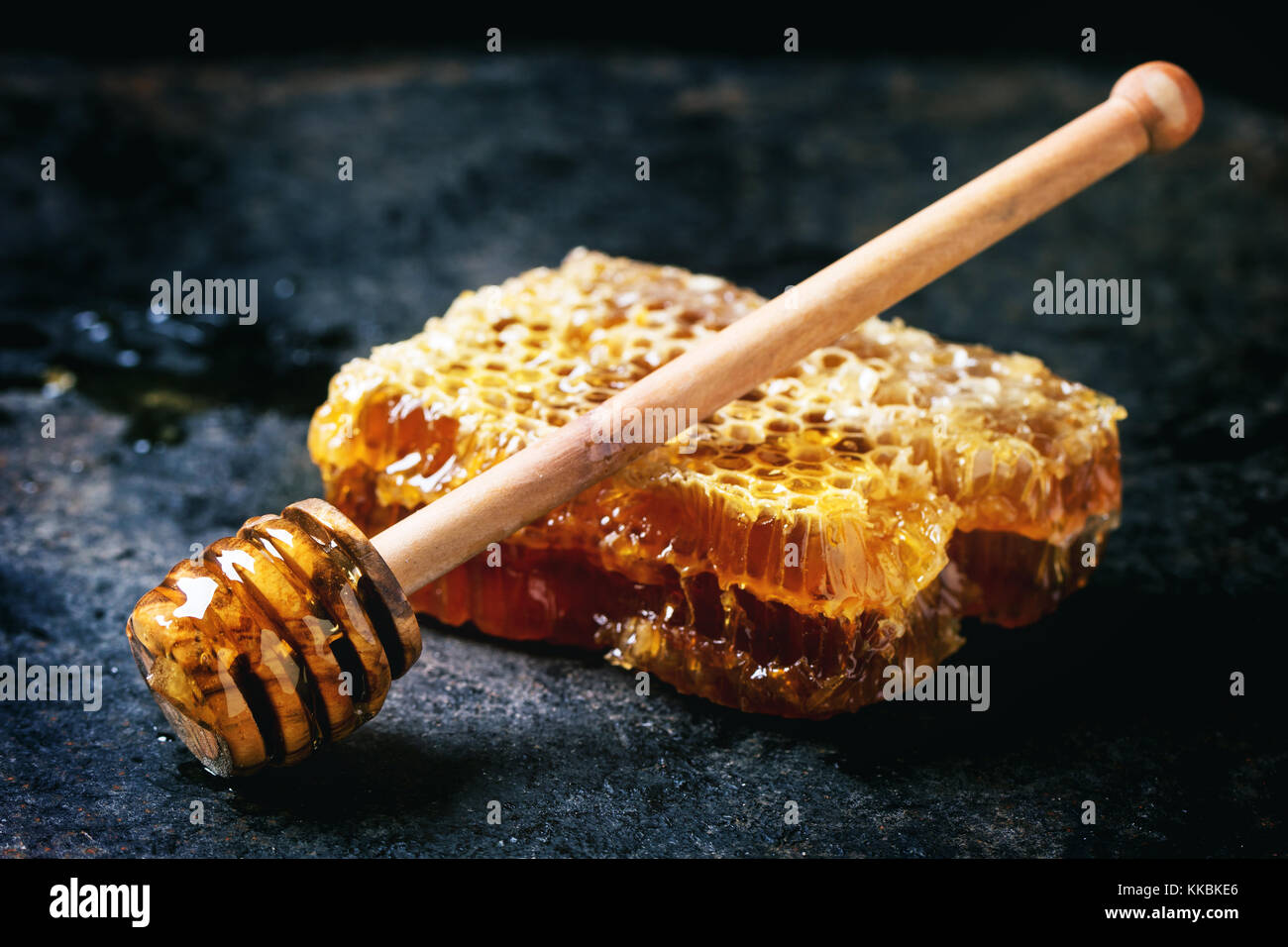 Honeycomb with honey dipper over black surface Stock Photo - Alamy