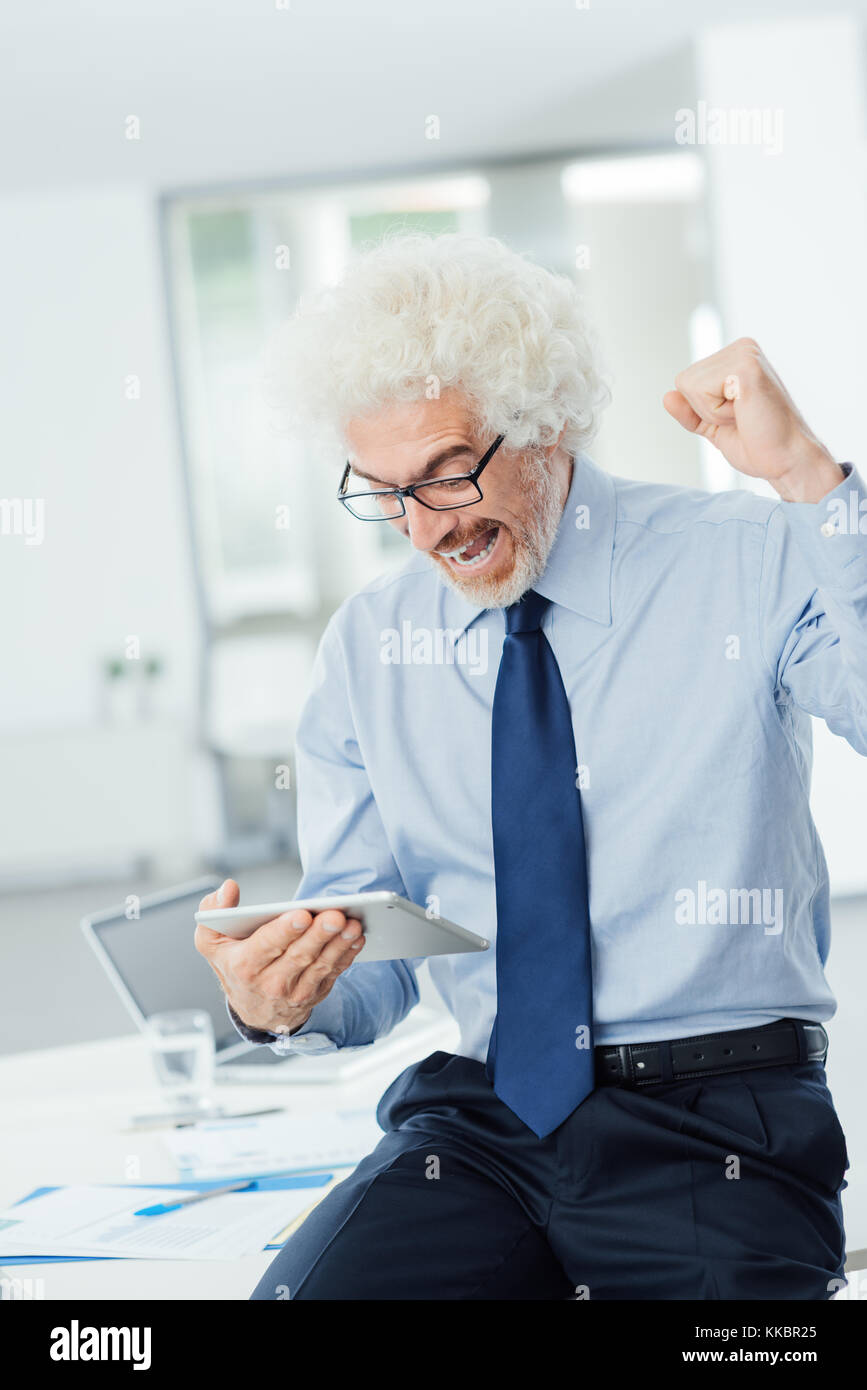 Cheerful successful business man with raised fist receiving good news ...