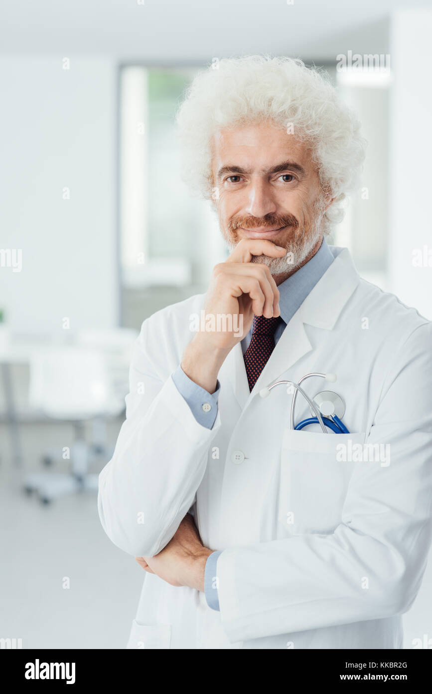 Professional doctor posing at hospital and smiling at camera with hand ...