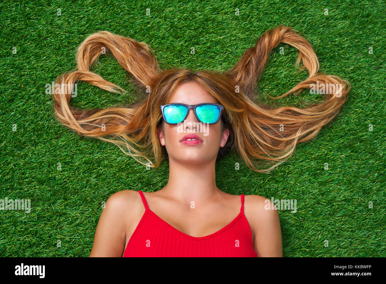 Blond teen girl with hair heart shapes lying down on turf with ...